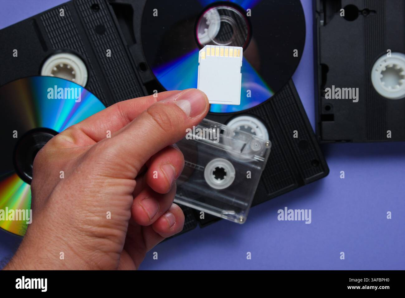 Hand holds SD memory card on the background of outdated storage media ...