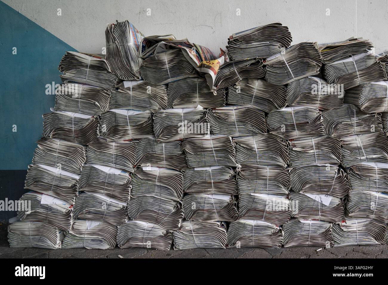 Bundles of newspapers are arranged at a wall in the street. The papers ...