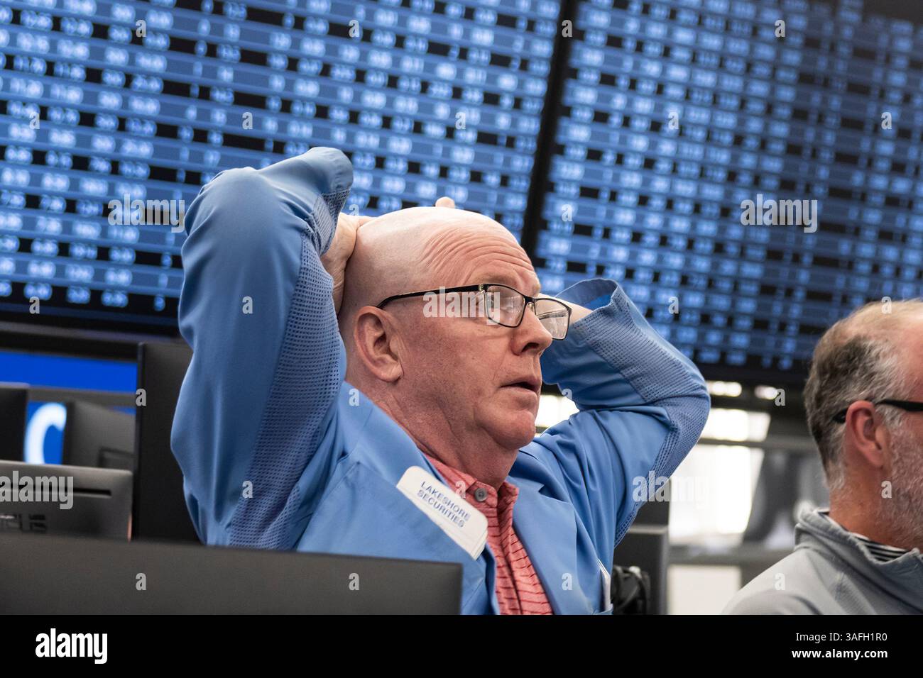 A trader holds his head as he watches global market data while working ...