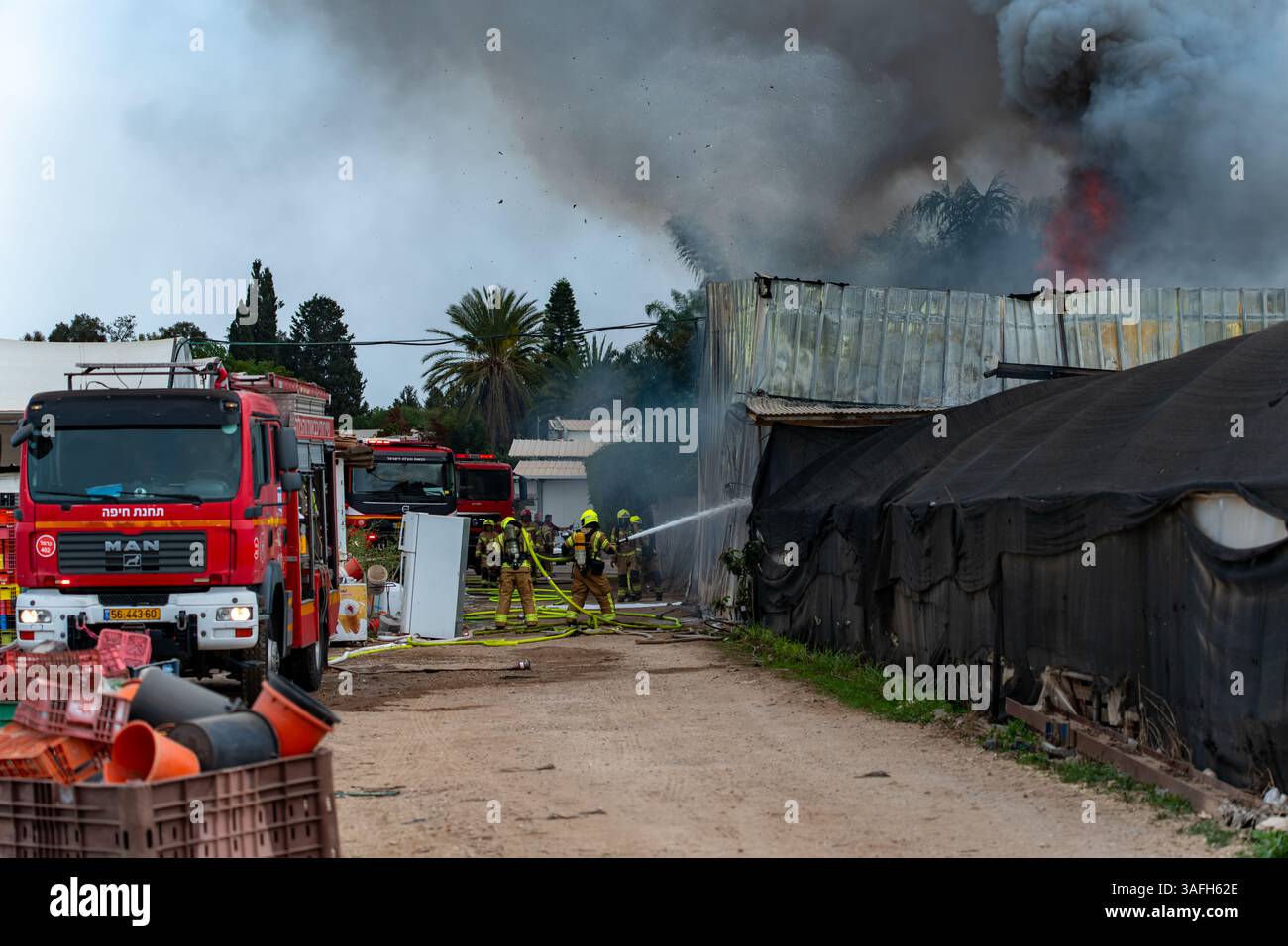 Firefighters extinguish a fire. Black smoke clouds and flames rise into ...