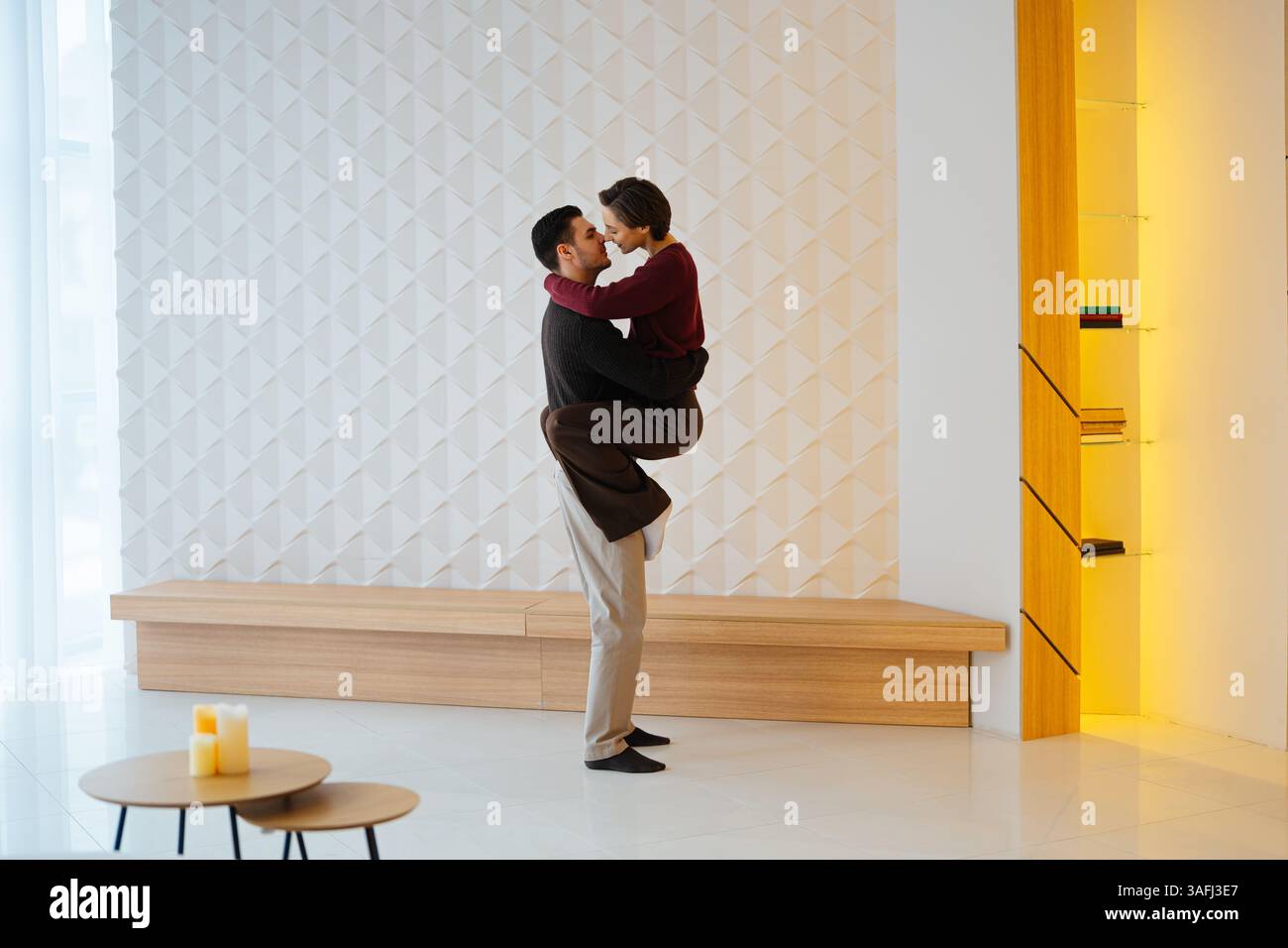 Romantic couple embraces in modern living room during afternoon light ...