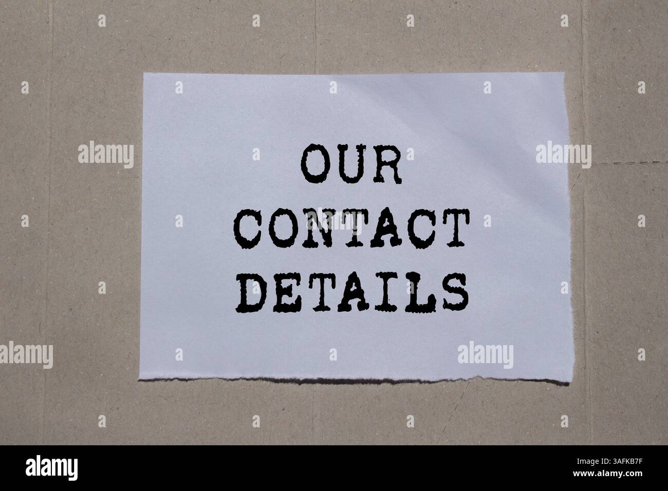 Our contact details message written on ripped torn paper on cardboard background. Conceptual our ...