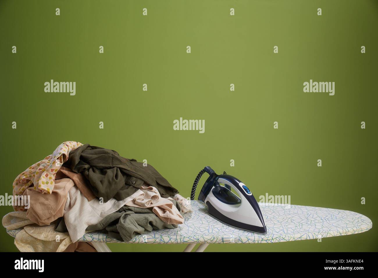 A close-up shows an iron near a pile of unfolded clothes on an ironing ...