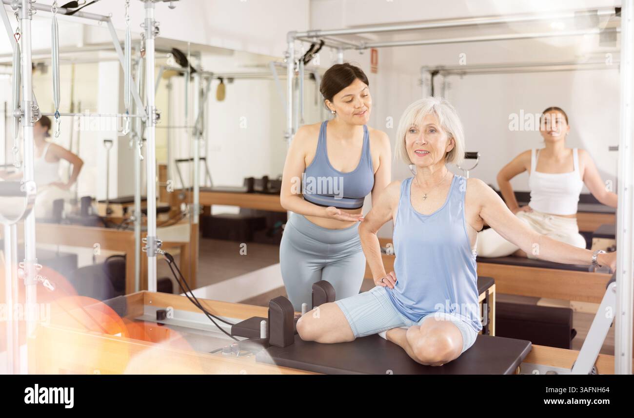 Female trainer checking and helping senior woman exercising on pilates ...