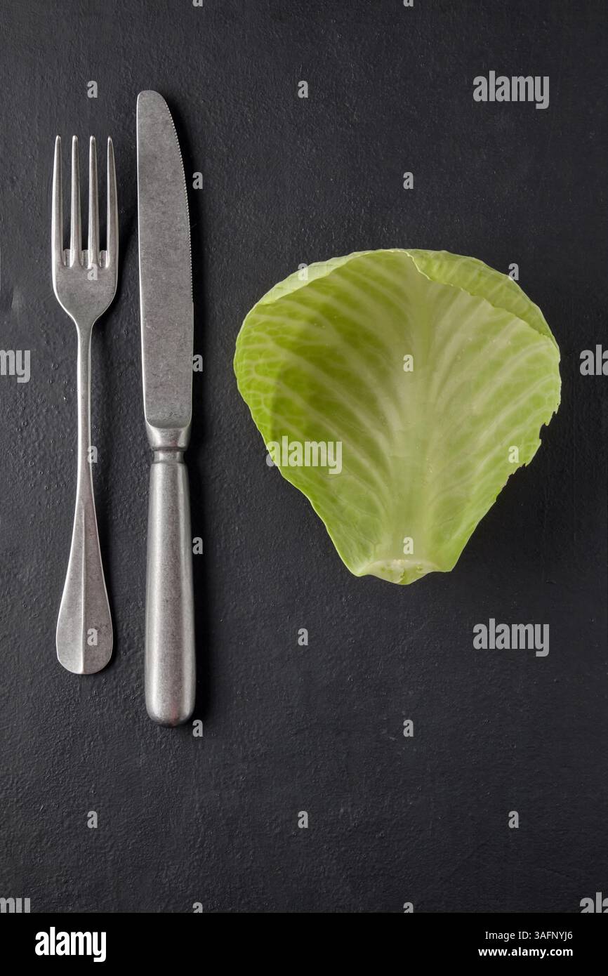 cabbage leaf and cutlery fork with knife on black table. weight loss ...