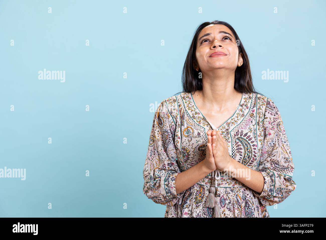 Wishful calm woman praying to jesus christ with folded hands in studio ...