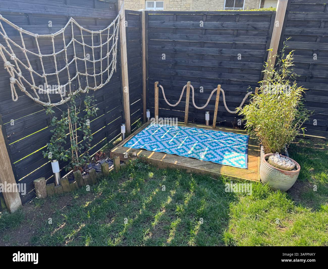 Pallet made deck in corner of shady garden with rope bannister and rope ...