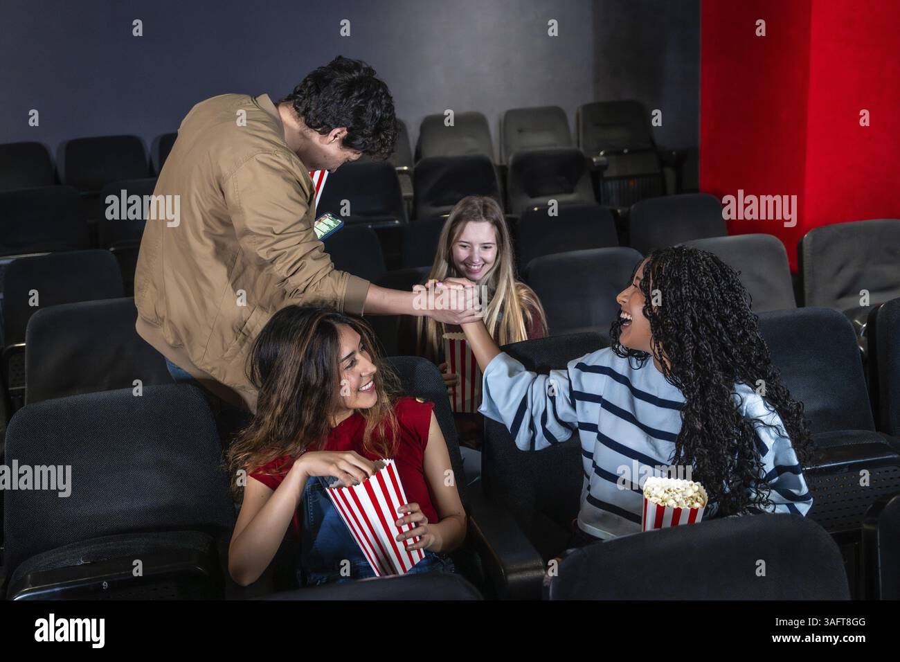 Friends enjoying popcorn and shaking hands while watching an exciting ...