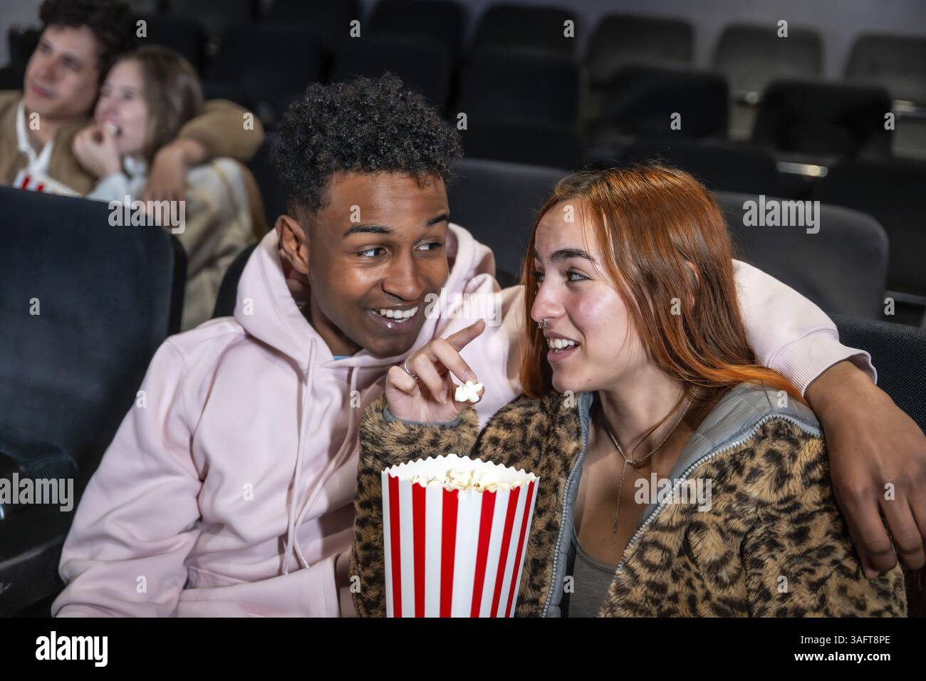 Happy diverse couple enjoying film and sharing popcorn bucket in movie ...