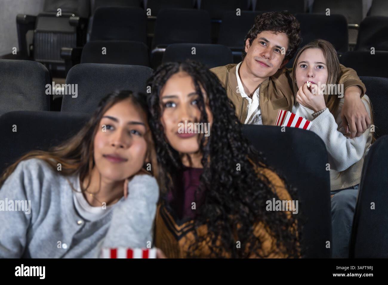 Group of friends enjoying a film at the movie theater, sharing popcorn ...