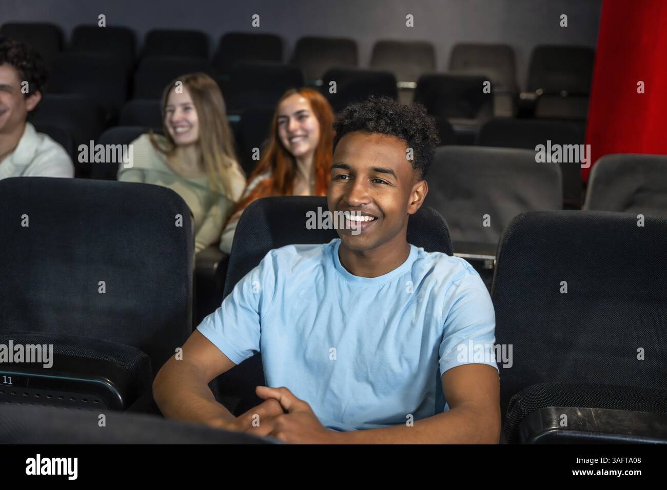 Young man smiles while watching a movie in a cinema, surrounded by his ...