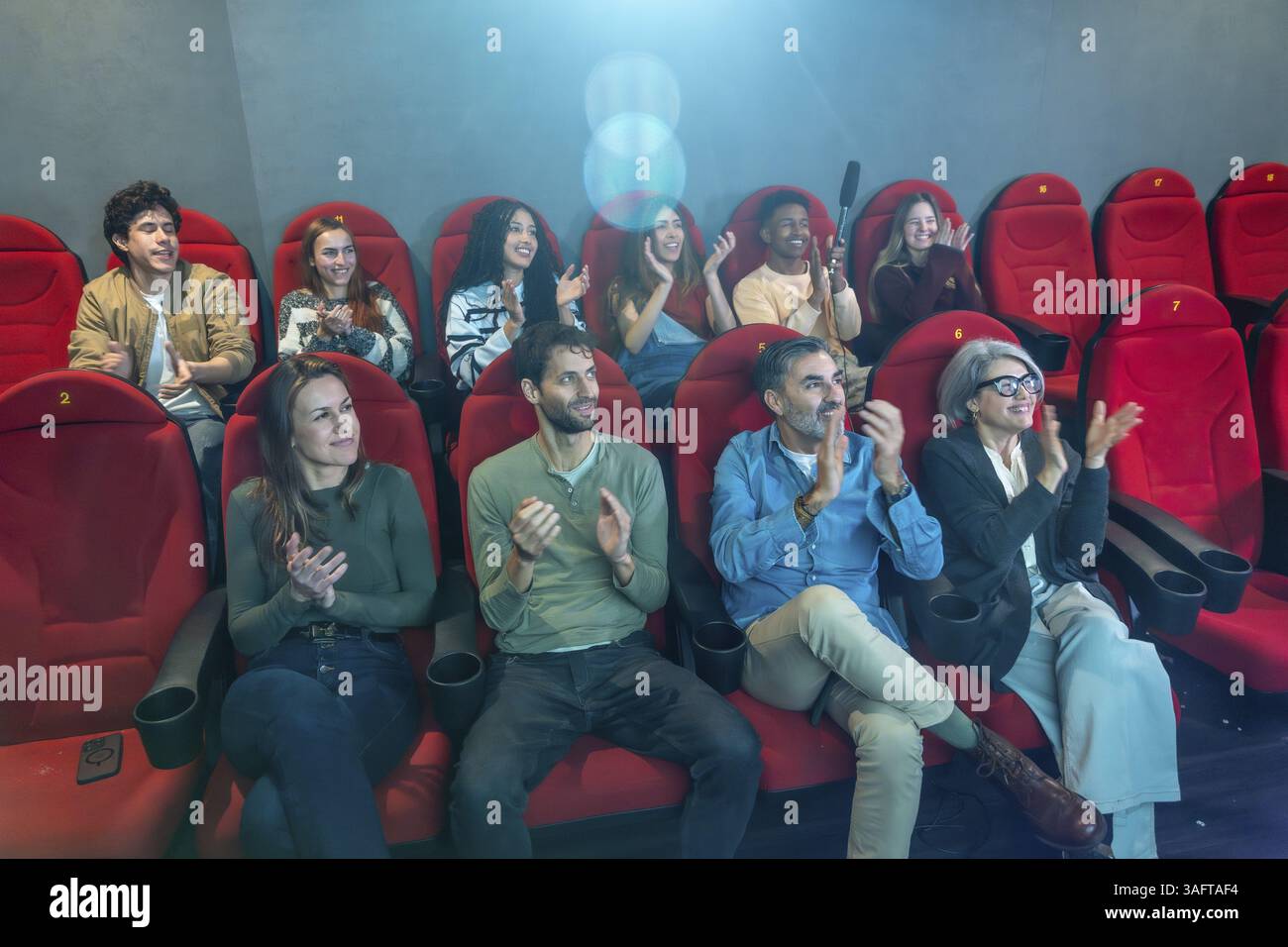 Diverse group of people clapping and enjoying a movie together in a cinema, creating a lively ...