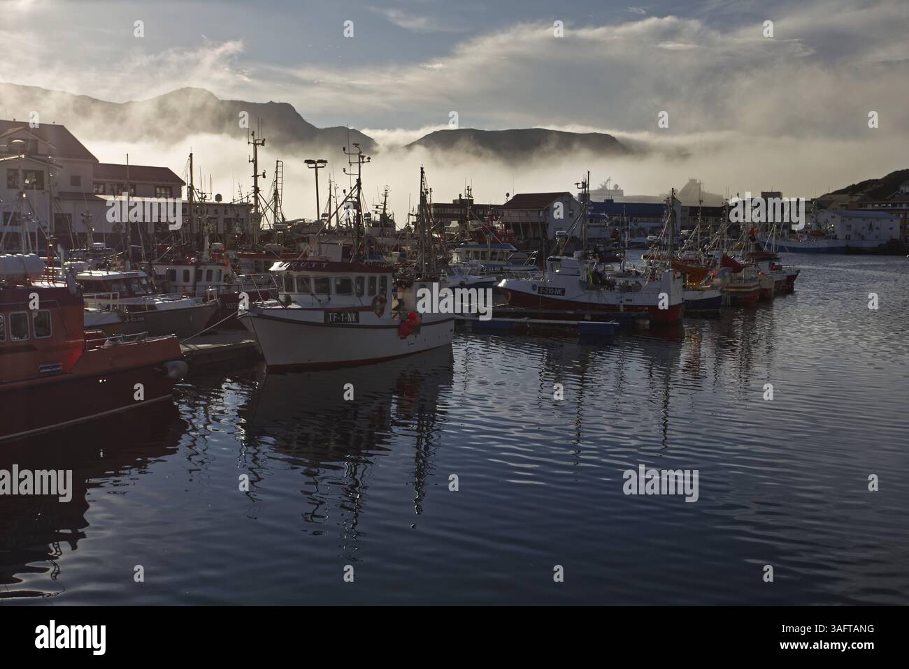 Fog over a harbour full of boats and surrounded by buildings ...