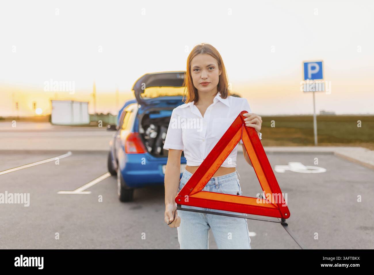 A woman holds a red warning triangle, indicating a car breakdown ...