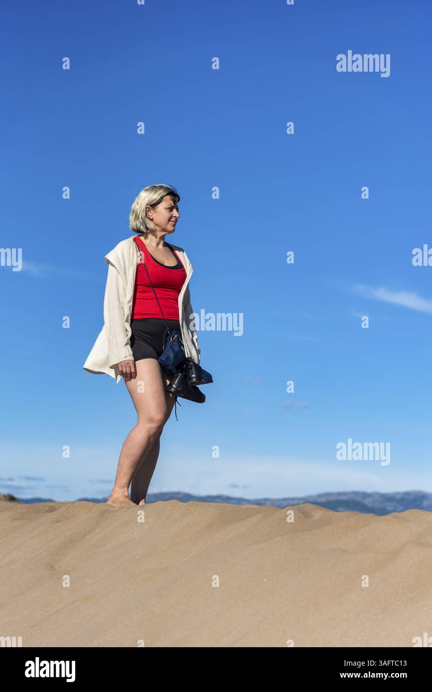 Woman enjoying freedom walking barefoot on sand dune carrying shoes ...