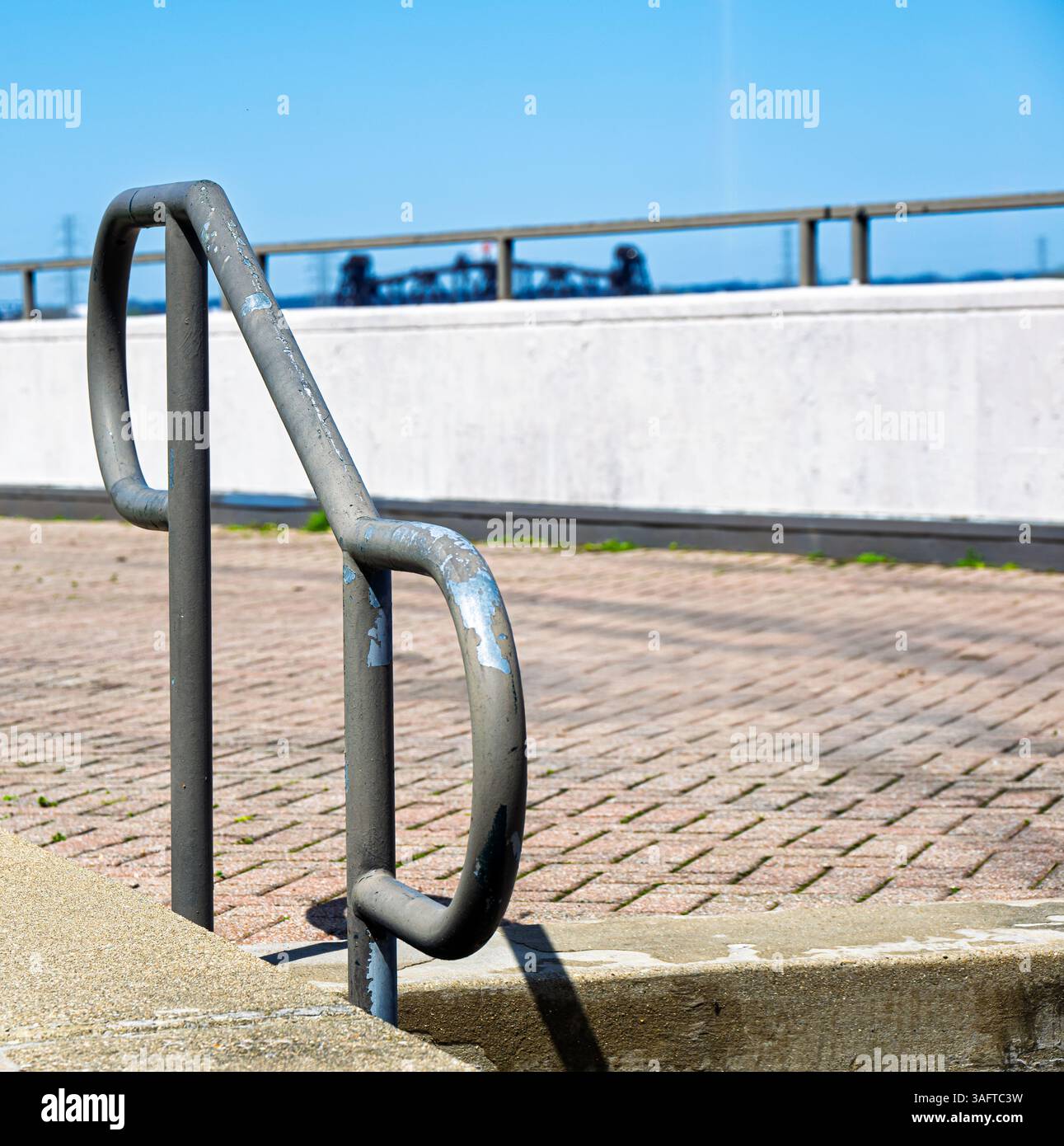 Metal stair railing leading to brick paved area by white concrete wall ...