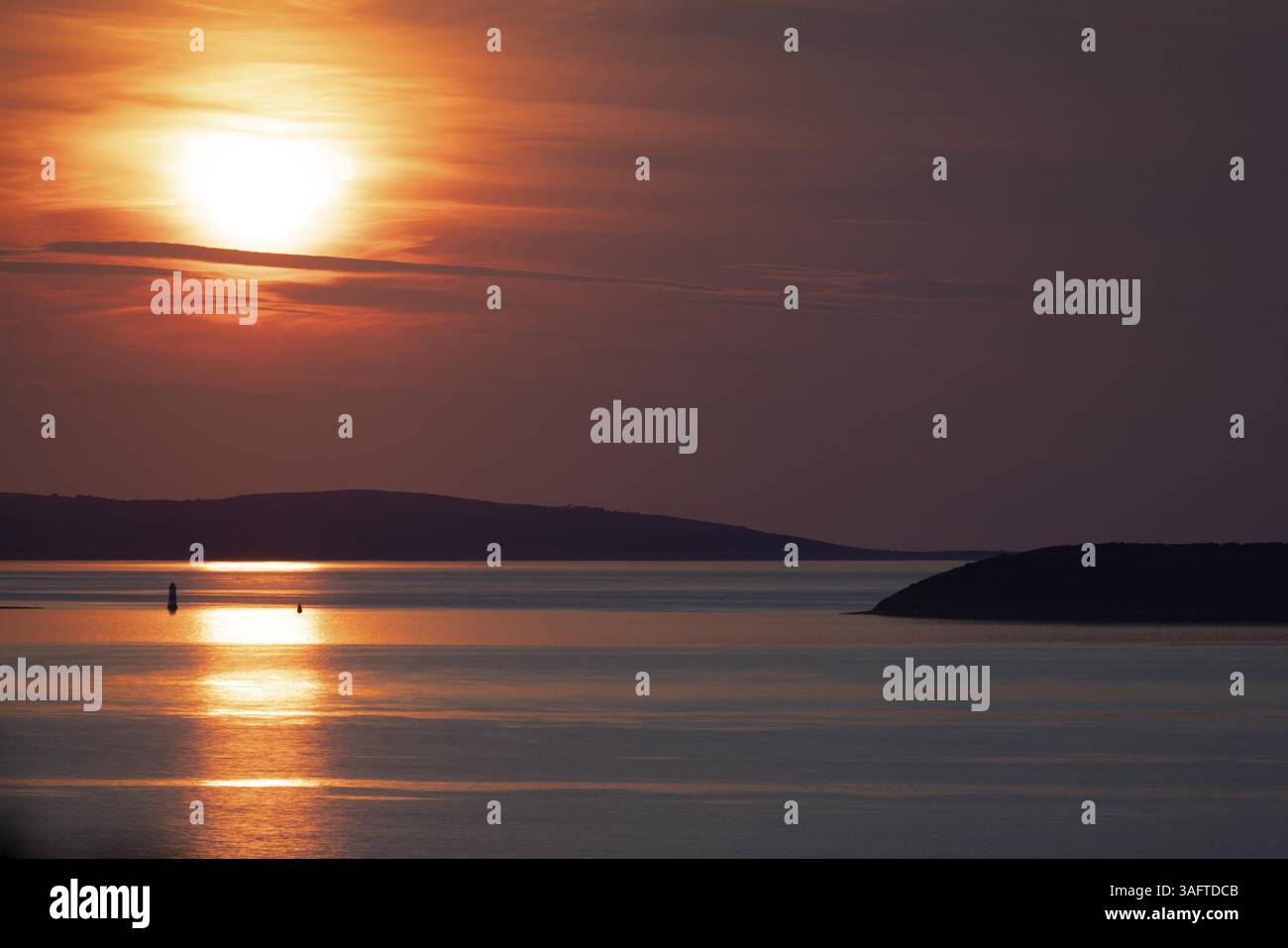 Sunset, sun sinks glowing red behind the islands of Anglesey and Puffin ...