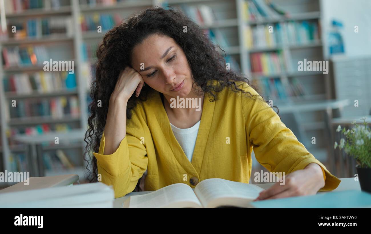 Tired Latino arabian woman sitting reading book studying knowledge exam ...