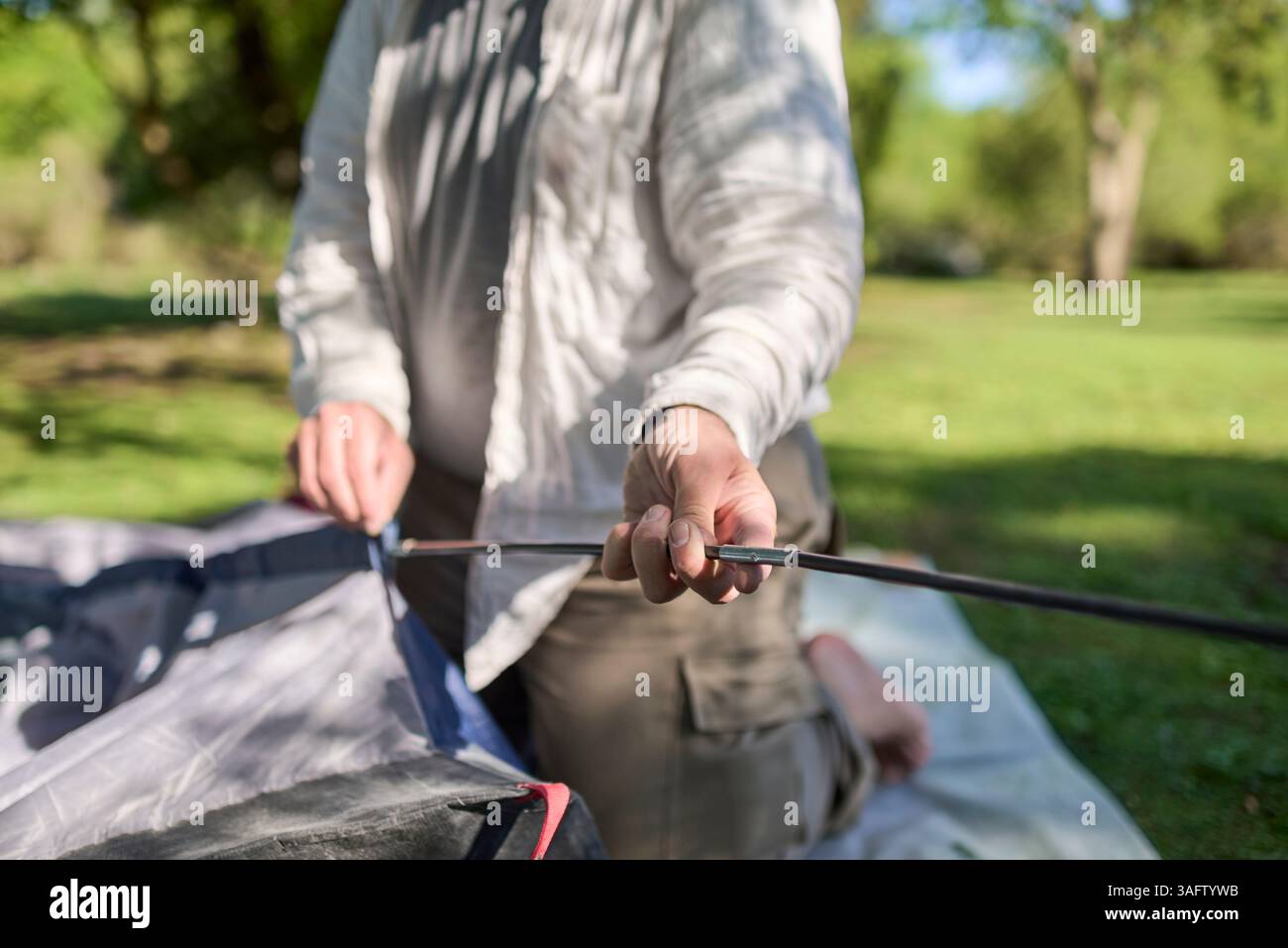 Unrecognizable man putting up the poles of his tent, in the process of ...