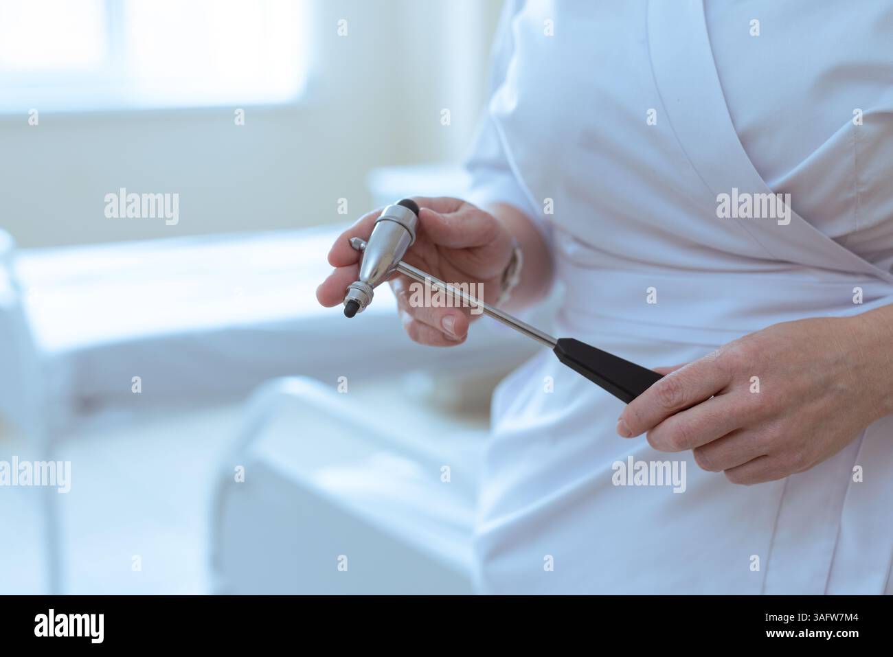 Doctor holding a reflex hammer in a medical room, preparing for ...