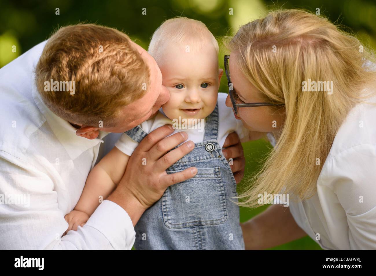 Mom, dad kiss and hug baby during walk in park, close up, showing love ...