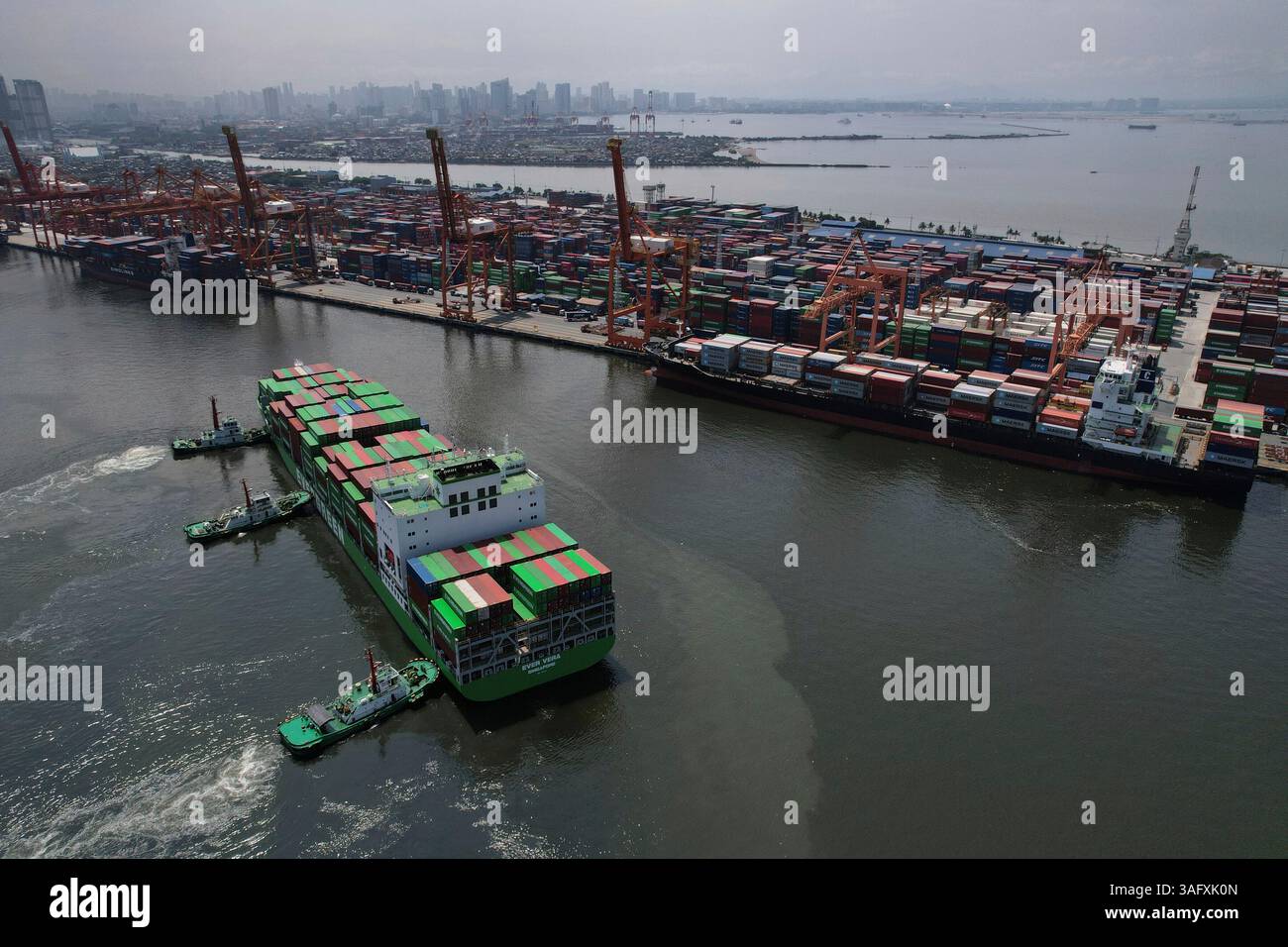 Tugboats assist a container ship as it prepares to dock at the Manila ...