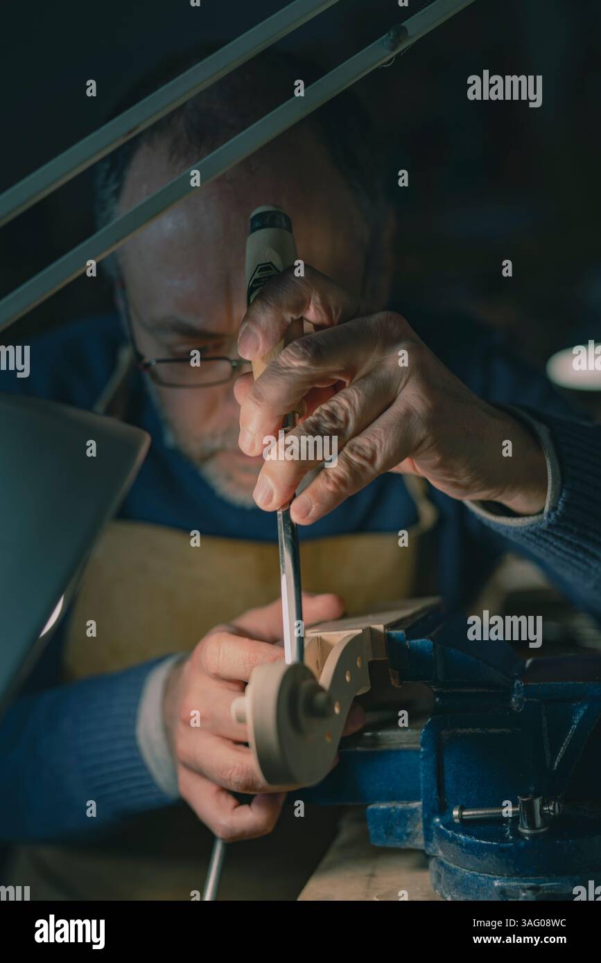 The image shows a Cremona violin maker carving a pegbox with a chisel ...