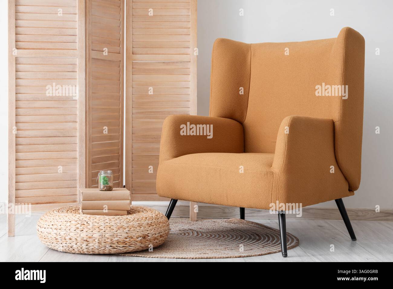 Comfortable armchair with folding screen and ottoman near white wall ...