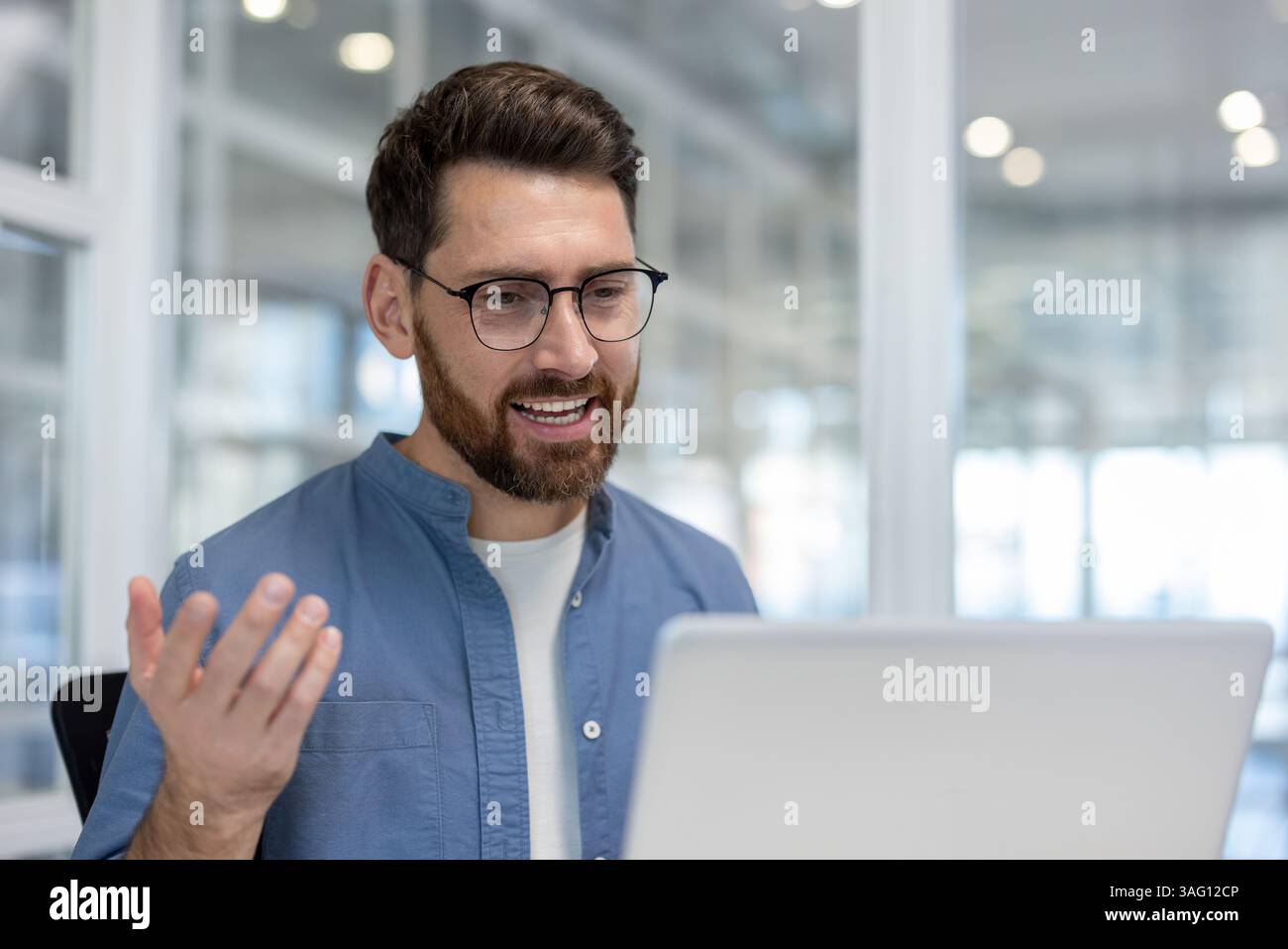 A cheerful man wearing glasses, engaged in a video call, expressing ...