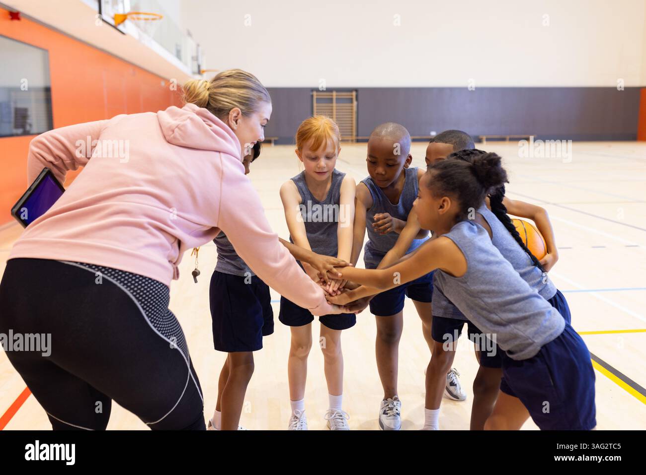 In school gym, female coach and diverse children huddling, showing ...