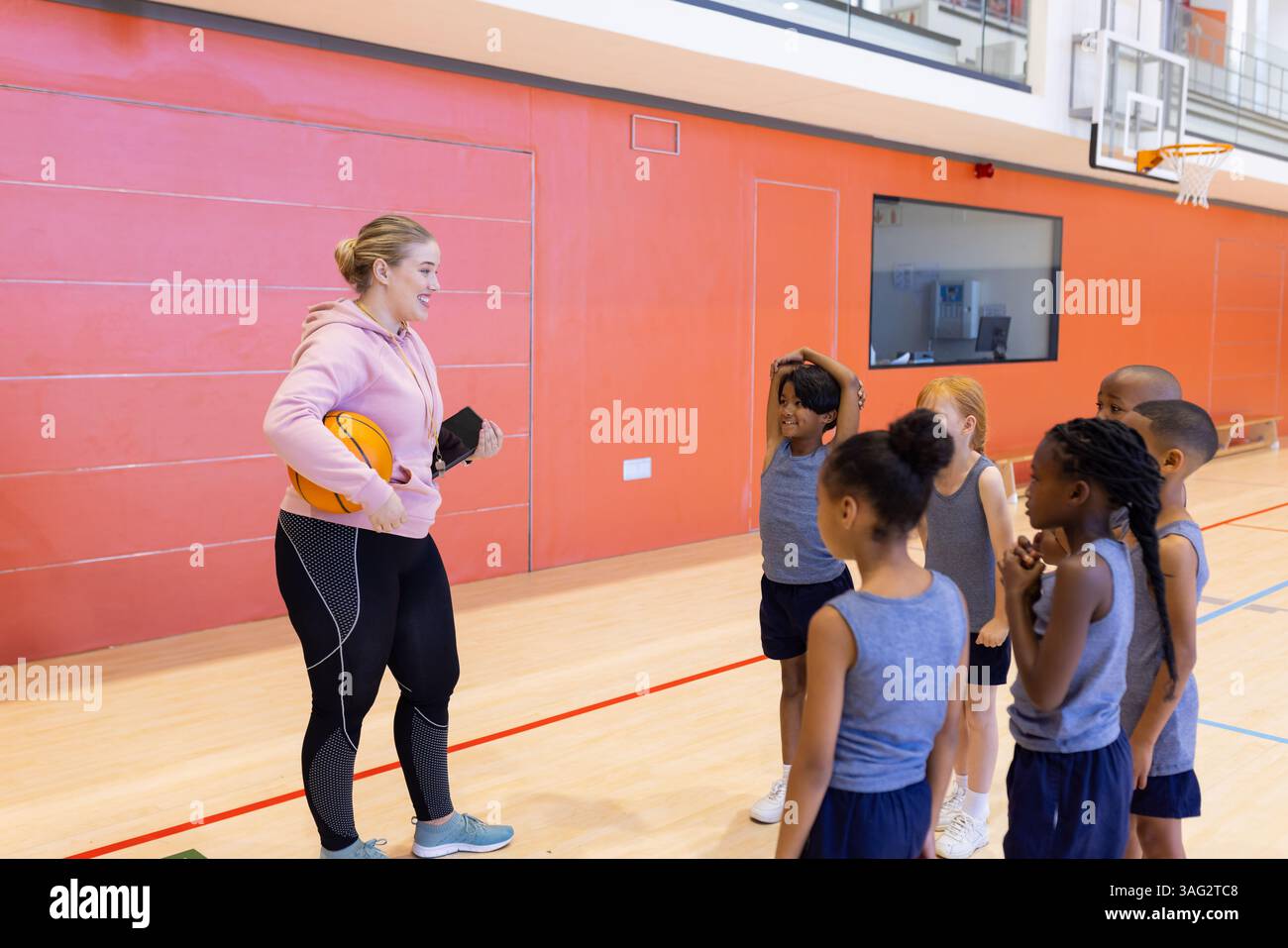 In school gym, female coach holding basketball and talking to group of ...