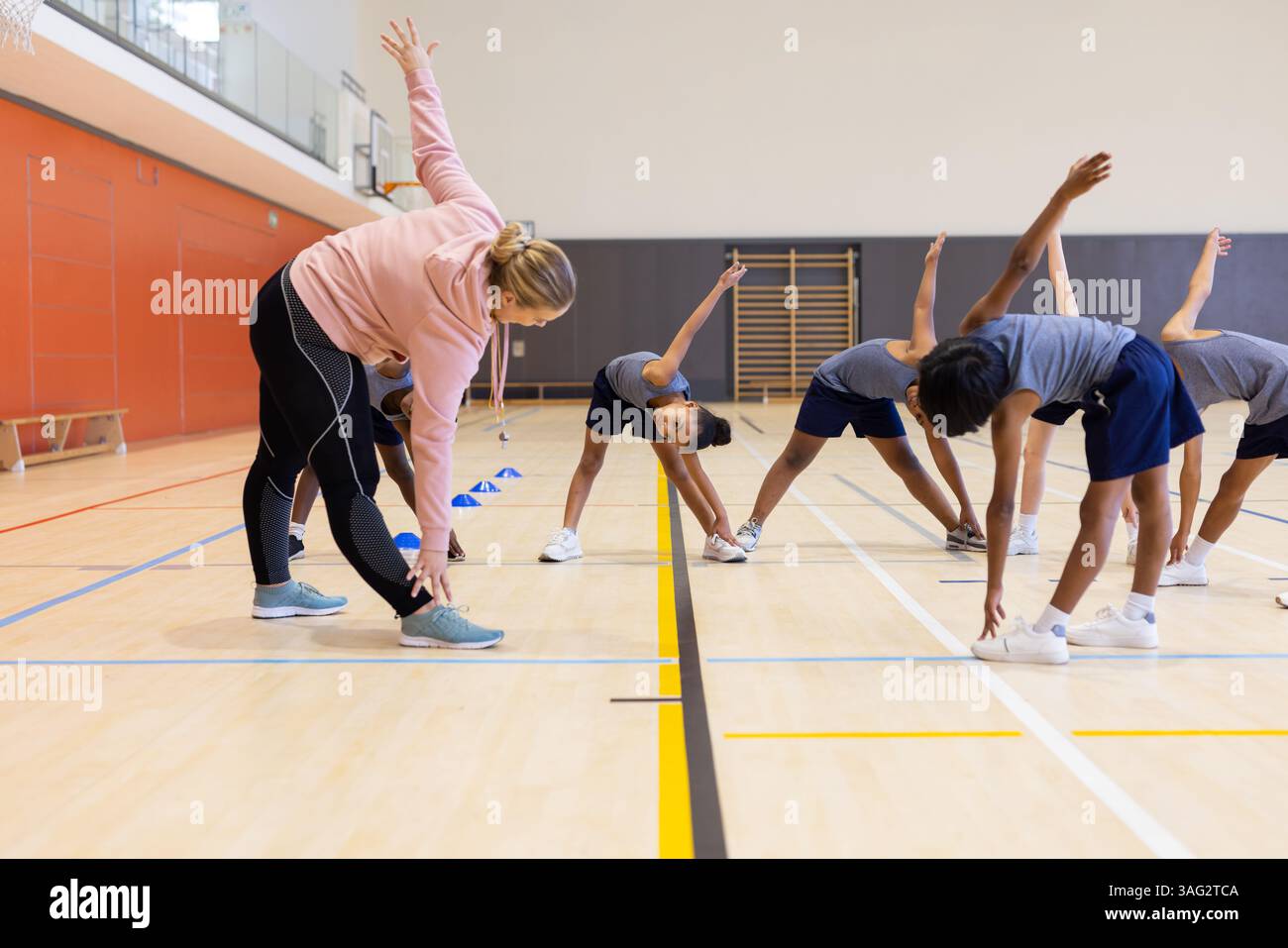 In school gym, female teacher leading group of diverse students in ...
