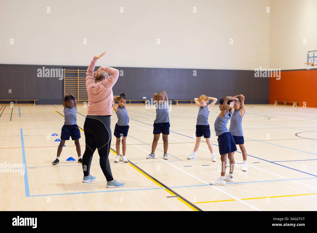 In school gym, diverse children stretching with female teacher during ...