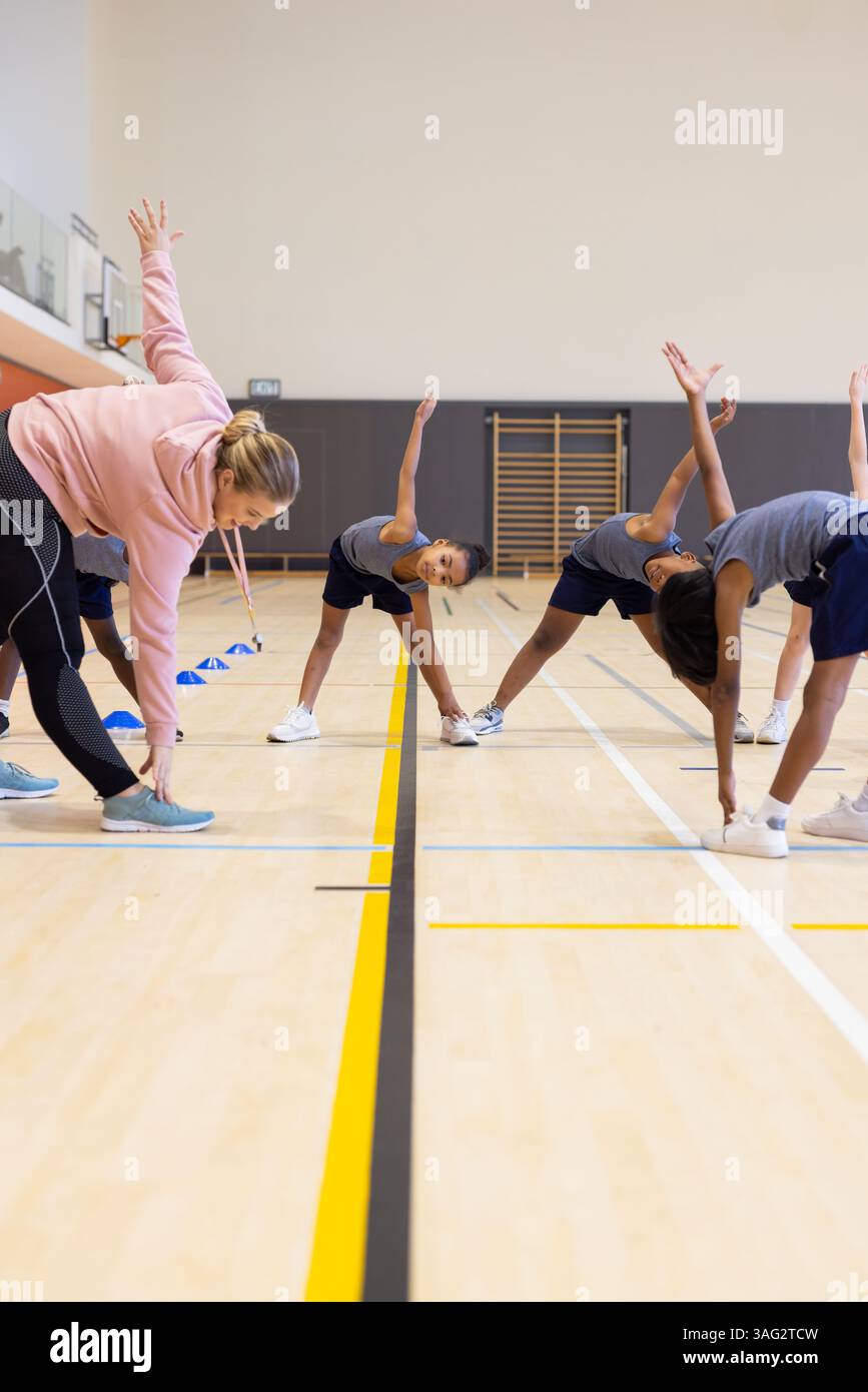 In school gym, physical education class, diverse students stretching ...