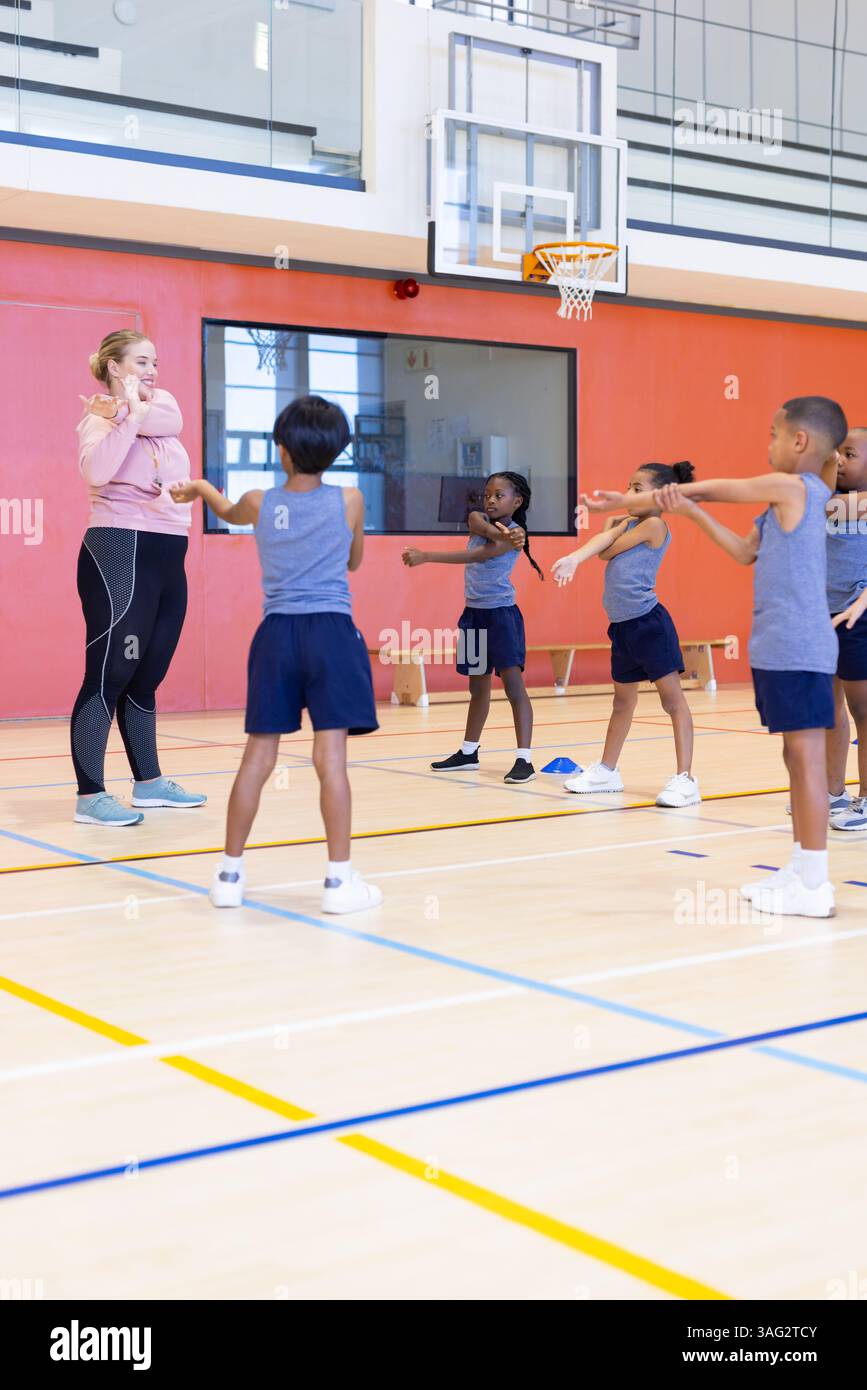 In school gym, diverse children exercising with female teacher ...