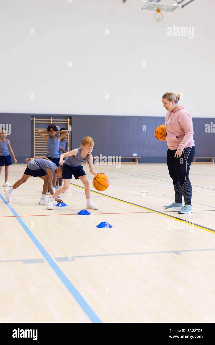 In school gym, diverse children practicing basketball drills with ...