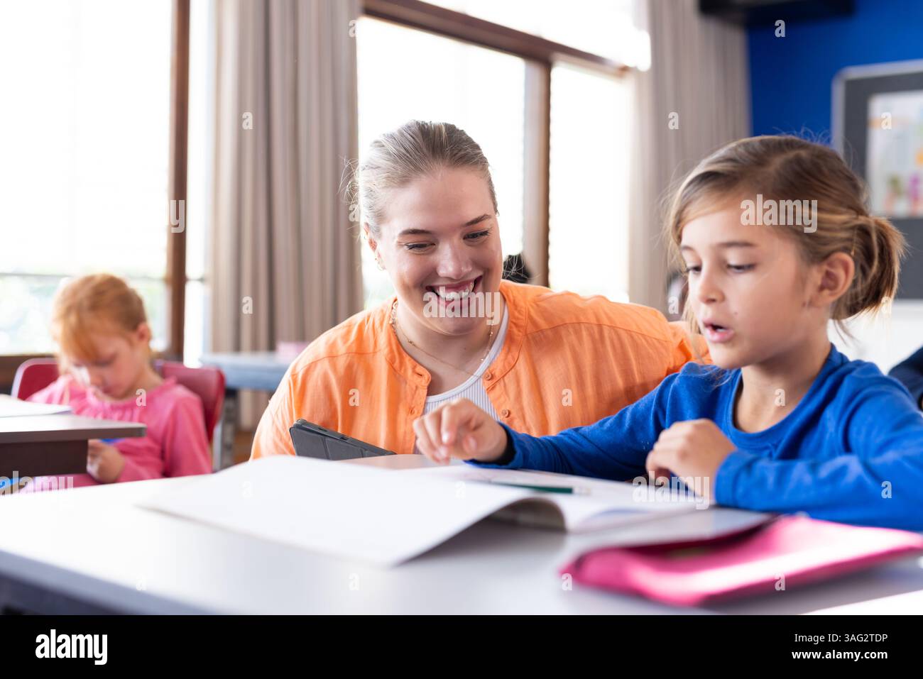 In school, female teacher helping boy with reading assignment in ...