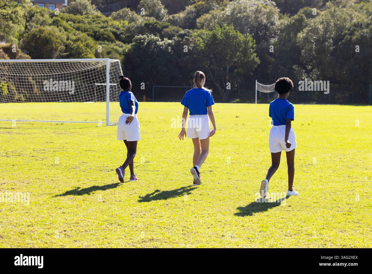 Walking on school field, three diverse girls in sports uniforms heading ...