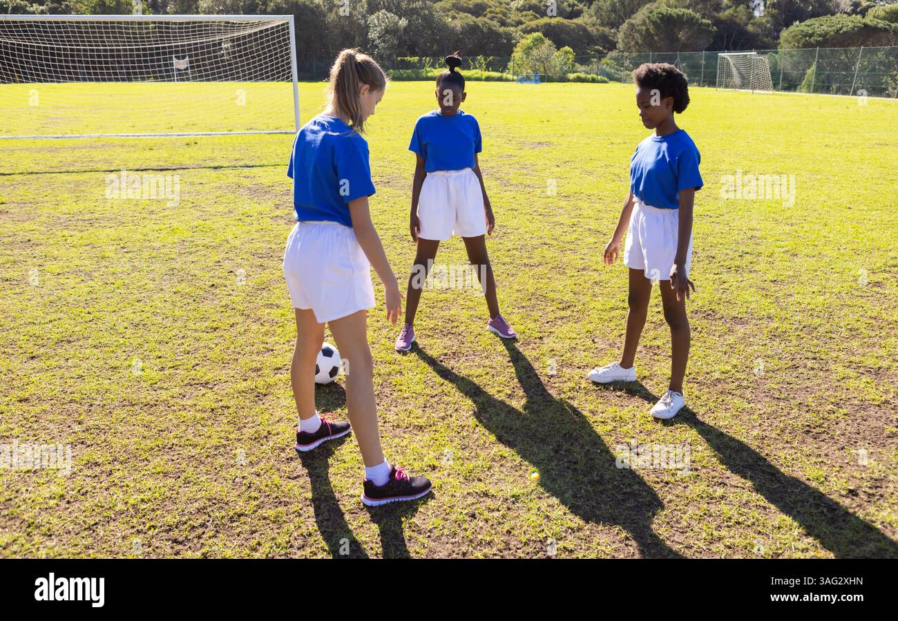 Playing soccer on school field, three diverse girls in sports uniforms ...