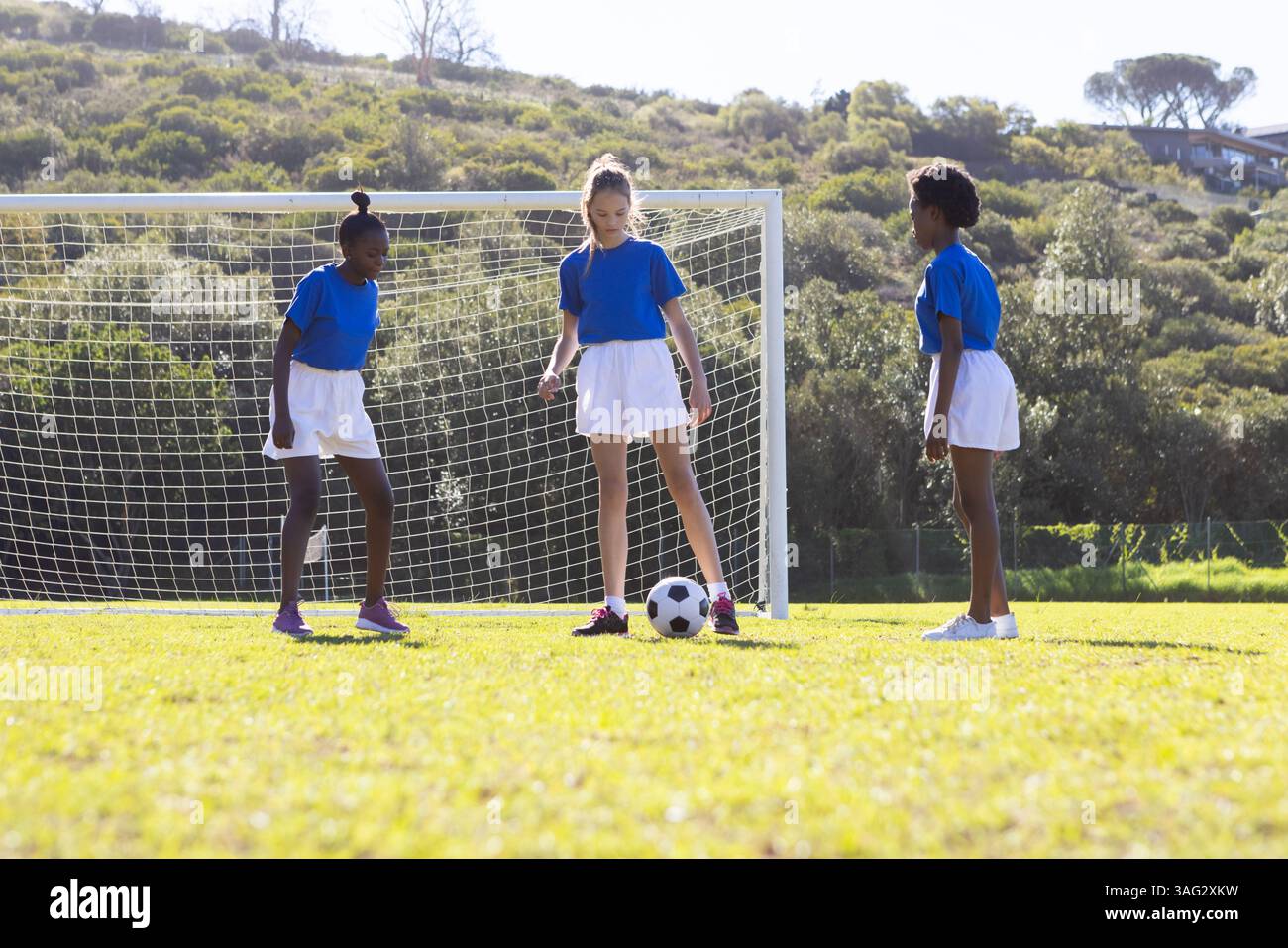 Playing soccer on school field, three diverse girls in sports uniforms ...