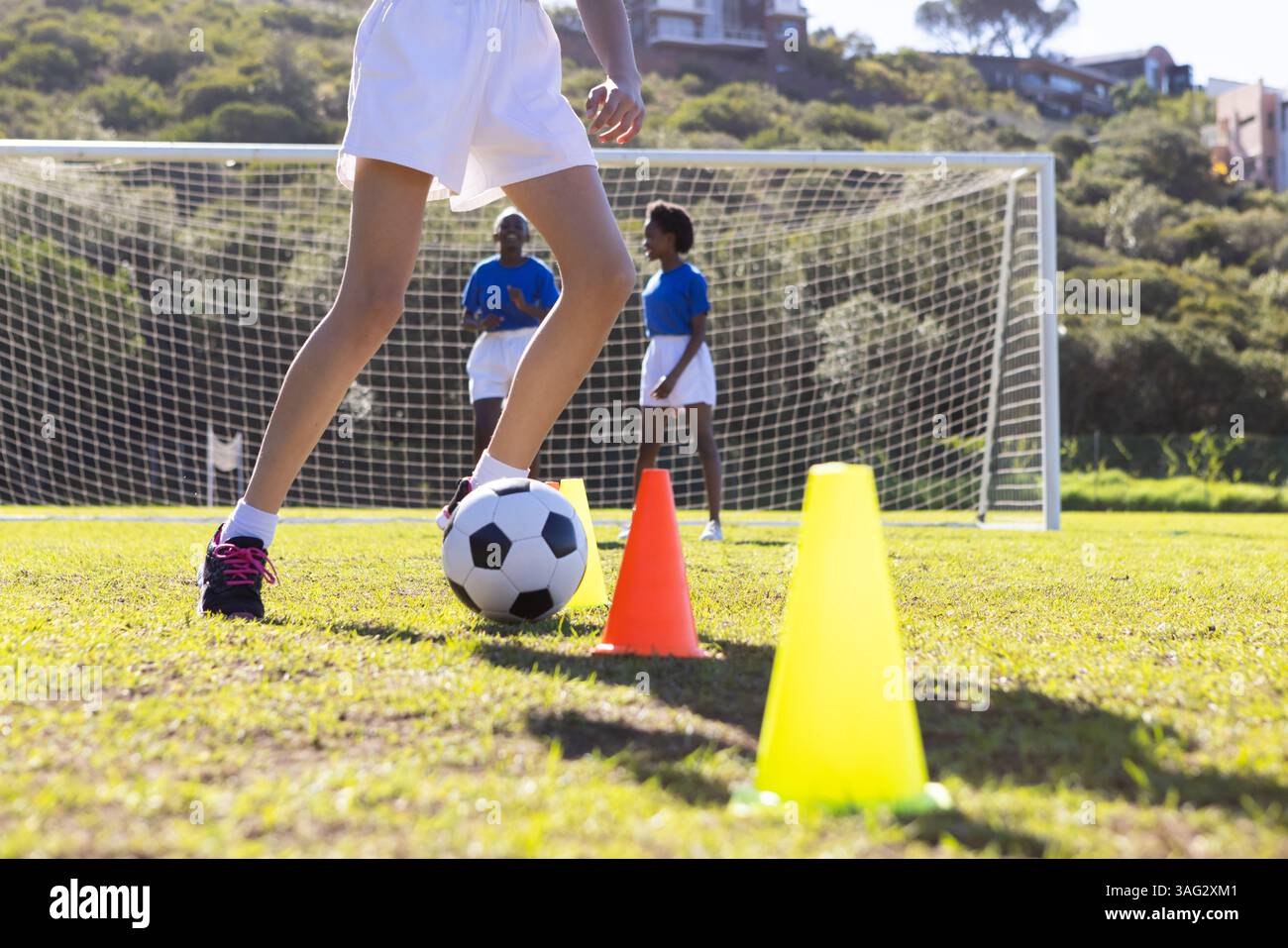 Playing soccer, diverse girls practicing dribbling around cones on ...