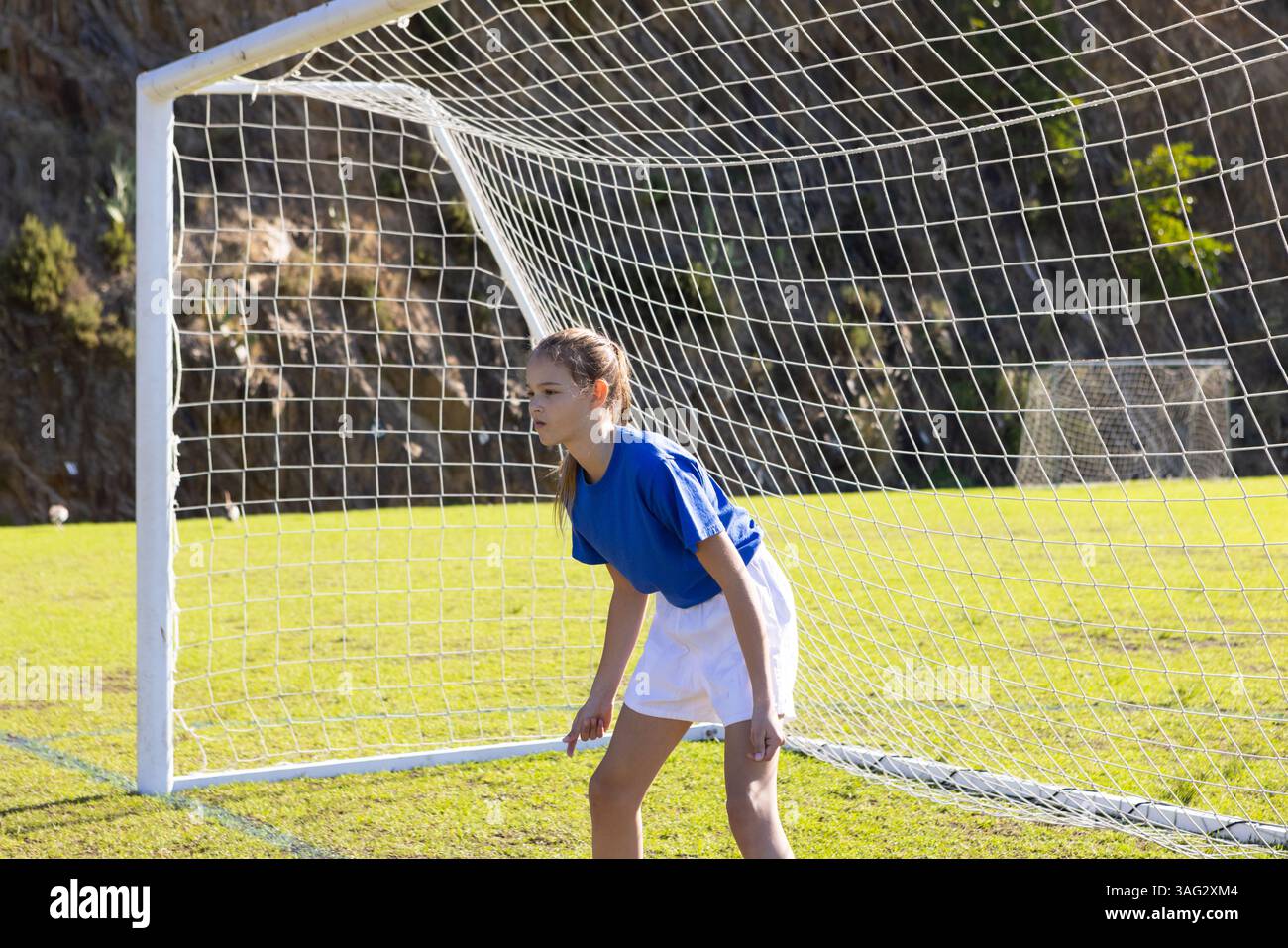 Playing soccer, girl in blue jersey standing as goalkeeper on school ...