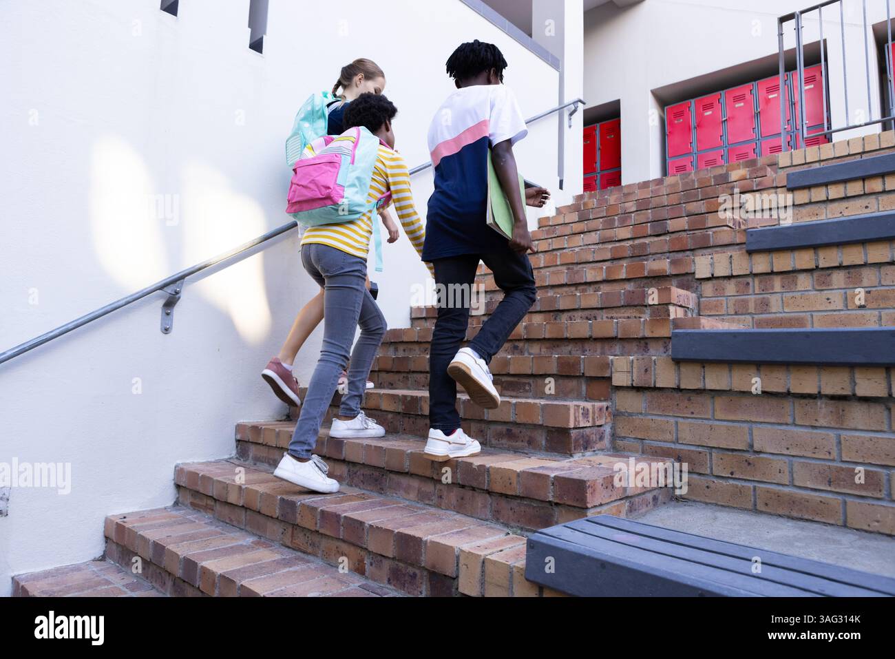 Diverse students with backpacks walking up stairs to school, heading to ...