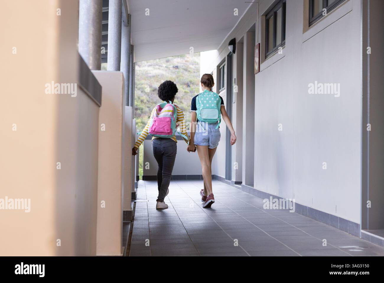 Walking in school hallway, two diverse girls with backpacks holding ...