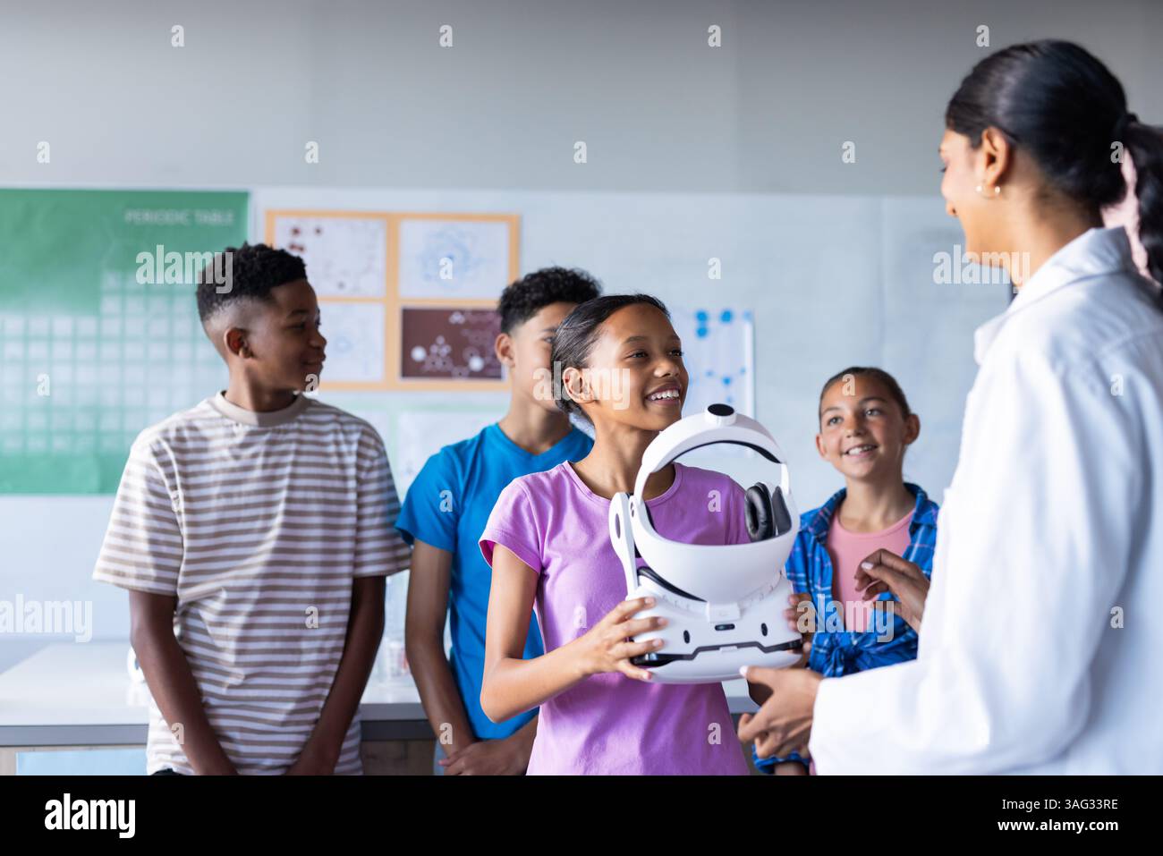 In school, students interacting with Indian female teacher while holding VR headset in classroom ...