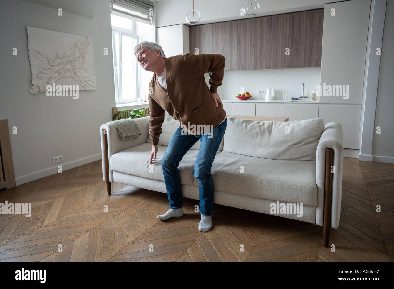 Struggling old man with severe back pain struggles to rise from couch ...