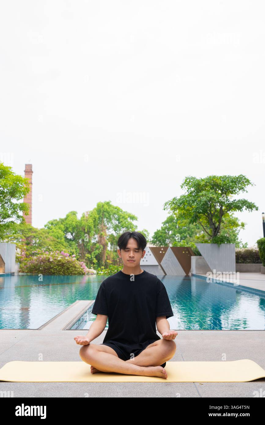 Young man doing yoga outdoors next to swimming pool during summer Stock ...