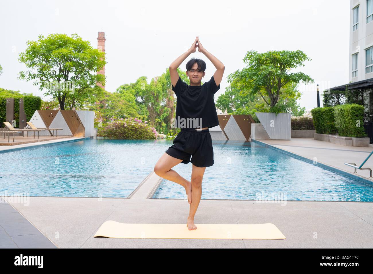 Young man doing yoga outdoors next to swimming pool during summer Stock ...