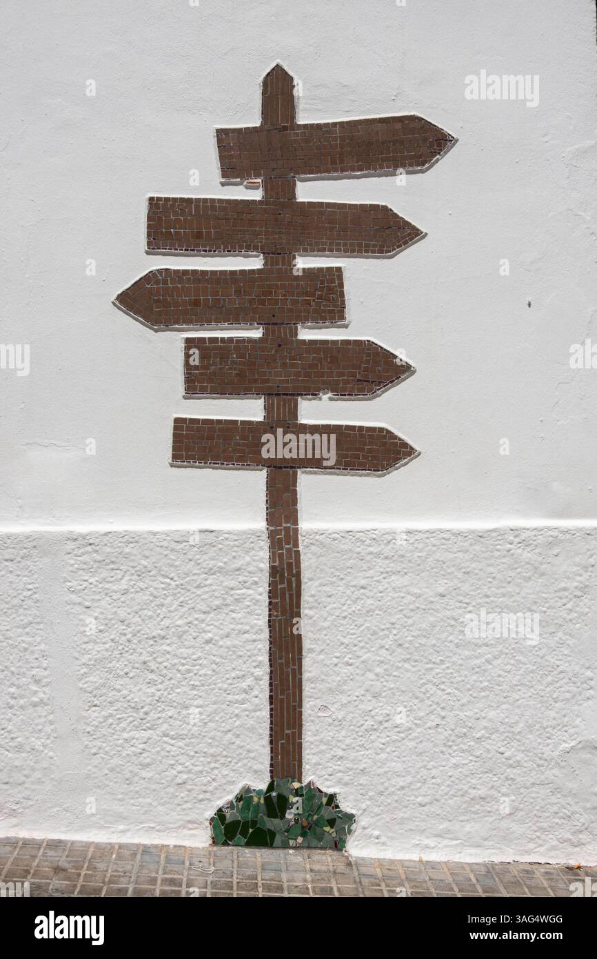 On a whitewashed wall, a mosaic tile signpost displays dates pointing ...