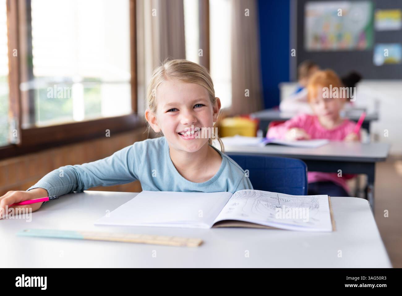 Smiling girl in school classroom drawing in notebook, sitting at desk ...